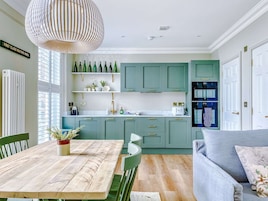 Cozinha moderna com armários verde-água, mesa de jantar de madeira e luminária pendente.