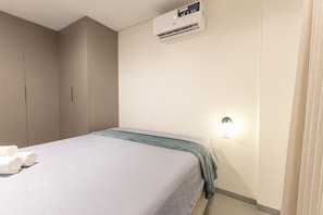 Quarto de hotel com uma cama, ar condicionado fixado na parede e uma luminária de cabeceira.