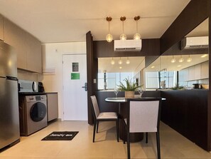 Uma cozinha moderna com máquina de lavar embutida, uma área de refeições com mesa redonda e cadeiras, e um espelho grande refletindo o ambiente.