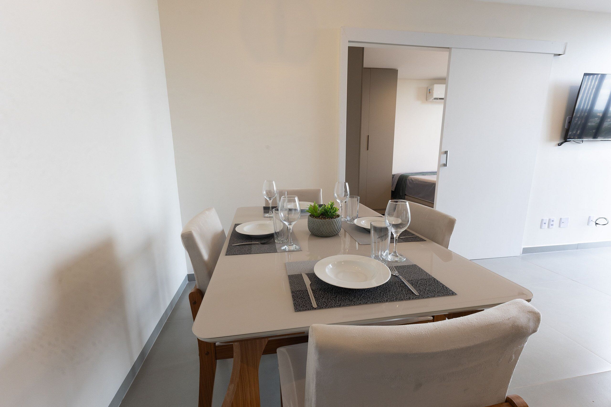 Uma área de refeições com uma mesa posta para quatro pessoas, incluindo pratos, talheres e copos.