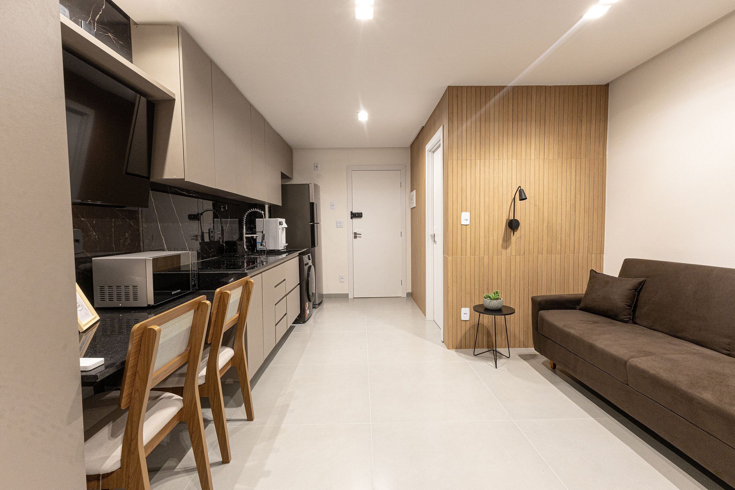 Um espaço de estar compacto com cozinha compacta, área de refeições com cadeiras, sofá e uma pequena mesa com uma planta.