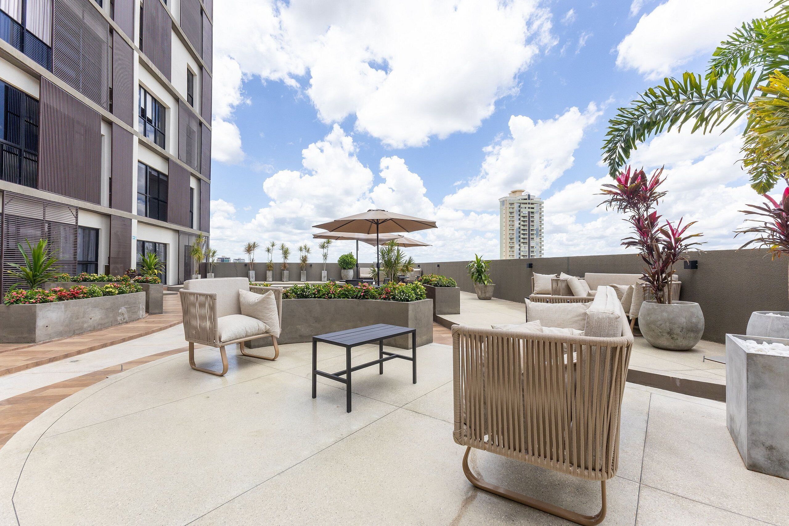 A rooftop patio with outdoor furniture, a table, and potted plants.