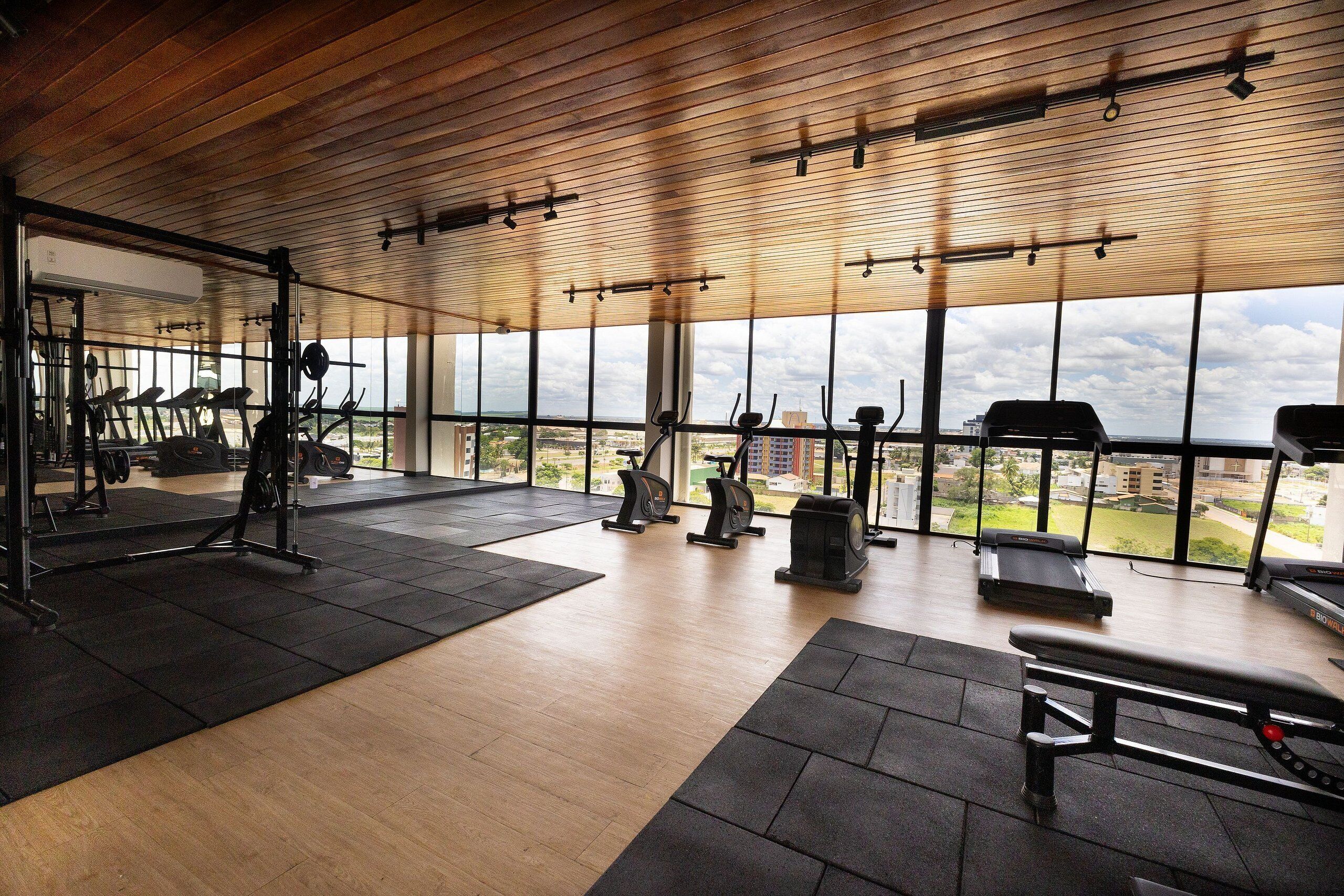 A gym with exercise equipment, large windows, and a wooden ceiling.