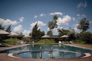 Piscina com espreguiçadeiras e guarda-sóis, rodeada por árvores e céu claro.