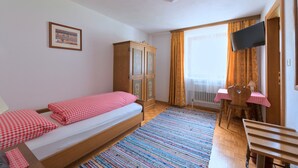 Quarto com cama, guarda-roupa, televisão e janela com cortinas.