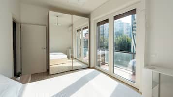 Quarto com uma cama grande, porta de correr com vidro para uma varanda e vista para edifícios.