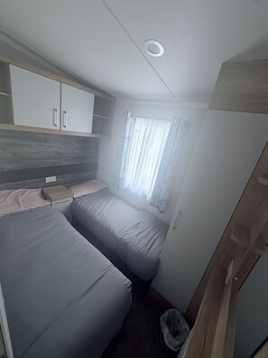 Quarto compacto com duas camas, um guarda-roupa e uma janela com cortinas.