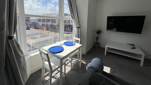 Uma sala de estar moderna com uma mesa de jantar, cadeiras, uma TV de tela plana e vista para a rua.
