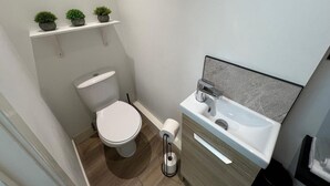 Uma casa de banho compacta com sanita, lavatório e três pequenas plantas em vasos numa estante sobre a sanita.