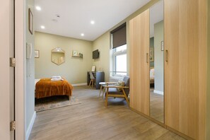 Um quarto com uma cama, uma escrivaninha, uma cadeira, uma televisão e um guarda-roupa.