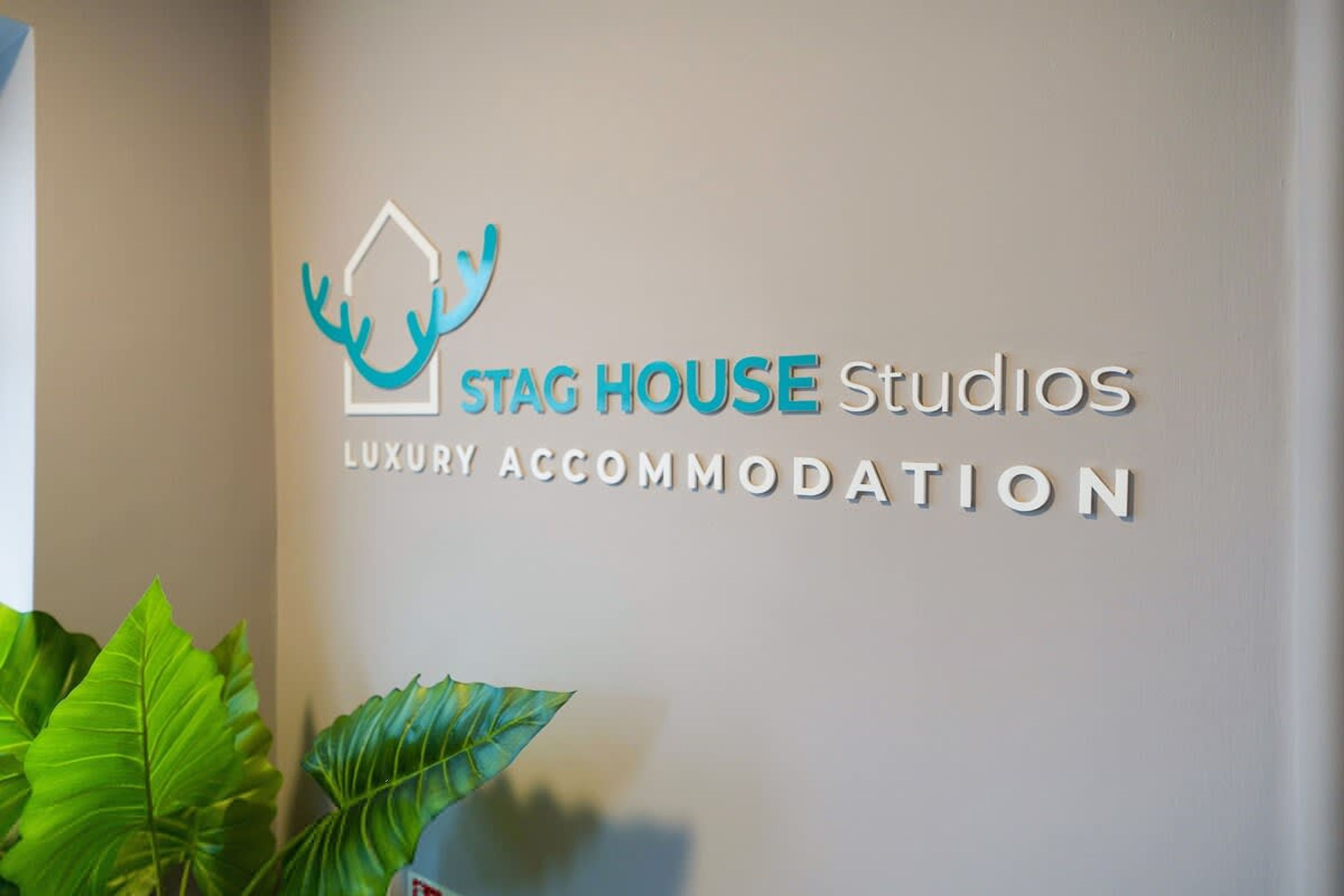 Uma parede com o texto 'STAG HOUSE Studios Luxury Accommodation' e o logotipo estilizado de uma casa.