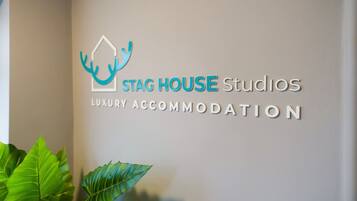 Uma parede com o texto 'STAG HOUSE Studios Luxury Accommodation' e o logotipo estilizado de uma casa.