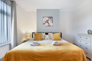 Quarto de hotel com cama, mesa de cabeceira, cômoda e janela com cortinas.