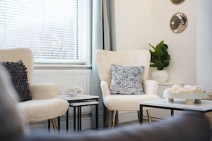 Uma sala de estar moderna com dois poltronas brancas, uma mesa de centro, uma mesinha de apoio e um vaso com planta.