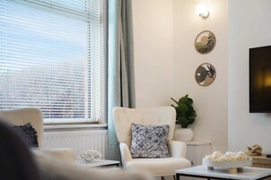 Uma sala de estar com uma poltrona branca, uma mesa lateral, um vaso de planta e decorações na parede.