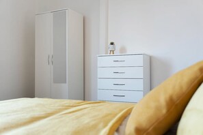 Um quarto com uma cama, um guarda-roupa branco e uma cômoda com gavetas.