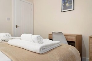 Quarto de hotel com cama, escrivaninha e cadeira. Há toalhas brancas dobradas sobre a cama.