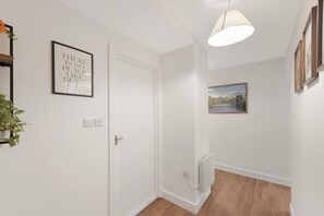 Um corredor com uma porta branca, uma moldura com uma citação na parede, um radiador e uma imagem de um castelo.