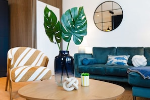 Uma sala de estar moderna com uma poltrona listrada, uma mesa de centro redonda, um sofá azul e plantas verdes grandes.
