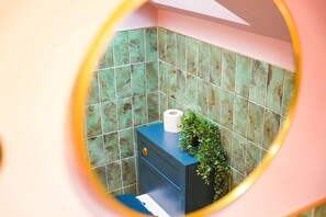Casa de banho com azulejos verdes, um armário azul e um rolo de papel higiénico.