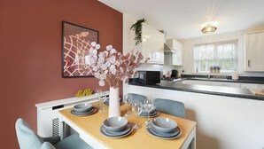 Uma cozinha moderna com armários brancos, uma mesa de jantar posta para quatro pessoas, com pratos, copos e um vaso de flores.