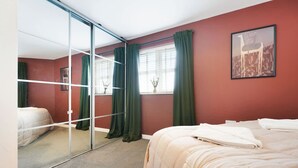 Quarto de hotel com cama, um espelho grande, janela com cortinas e um quadro na parede.