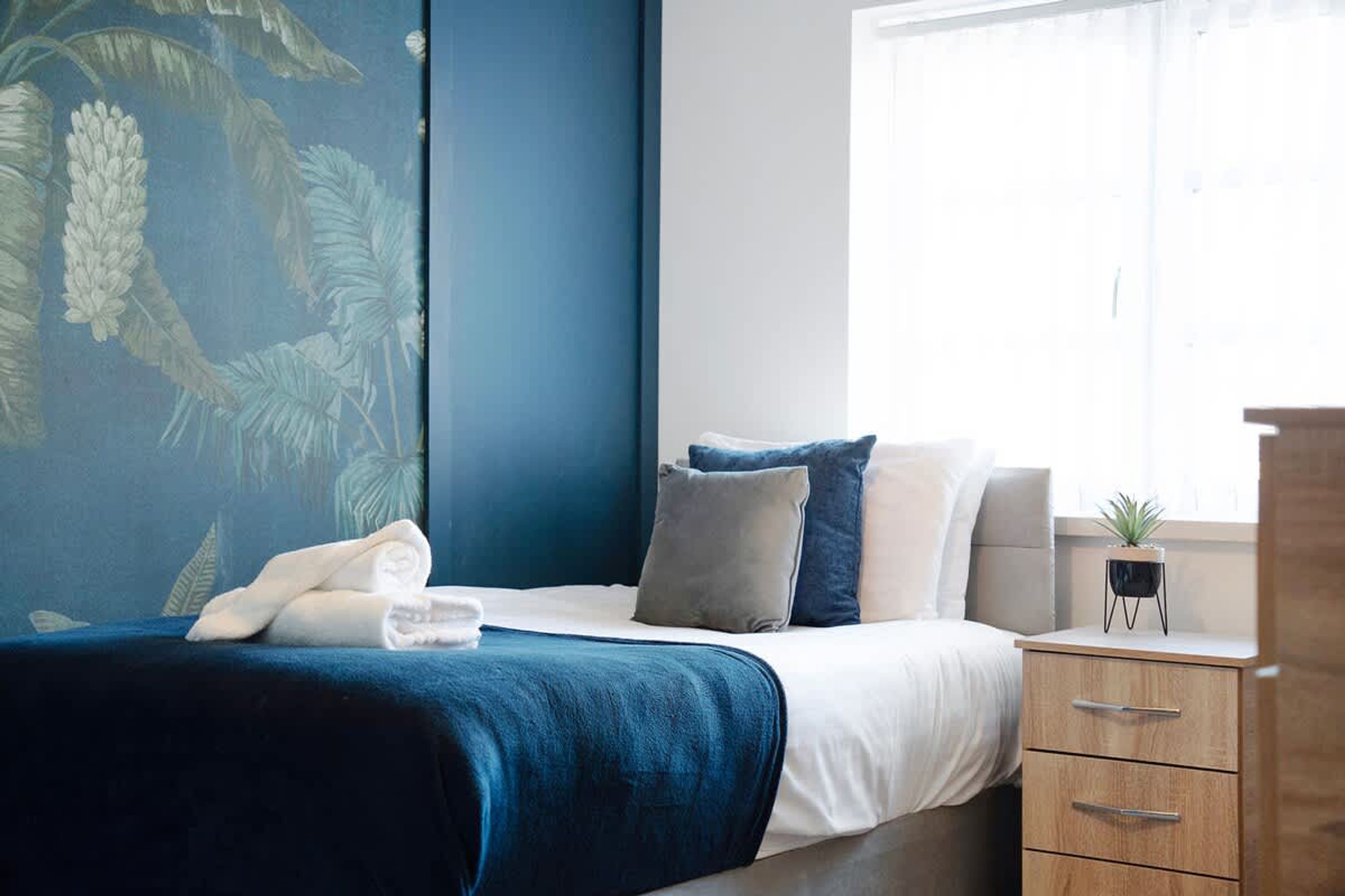 Quarto de hotel com cama, mesa de cabeceira, cômoda e janela.