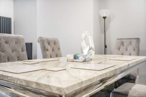 Uma mesa de conferência com tampo de mármore, rodeada por cadeiras estofadas, num espaço com parede lisa e um abajur.