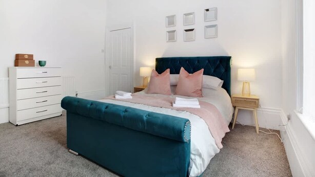 Um quarto com cama, cômoda, mesa de cabeceira e porta.