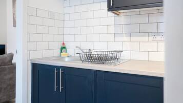 Cozinha com painel de azulejos brancos, armários azul escuro, pia de aço inoxidável e escorredor de louça.