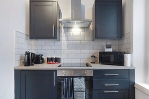 Cozinha moderna com armários escuros, exaustor de aço inoxidável, micro-ondas e chaleira.