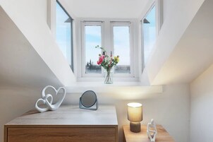 Quarto com claraboia, mesa de cabeceira com abajur e um vaso com flores.