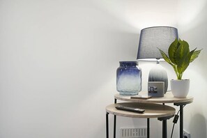 Uma pequena mesa com abajur, planta em vaso, vaso de flores e controle remoto.