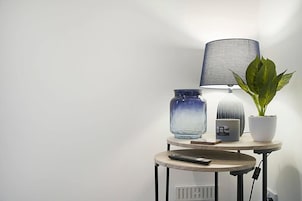 A small table with a lamp, a potted plant, a vase, and a remote control.