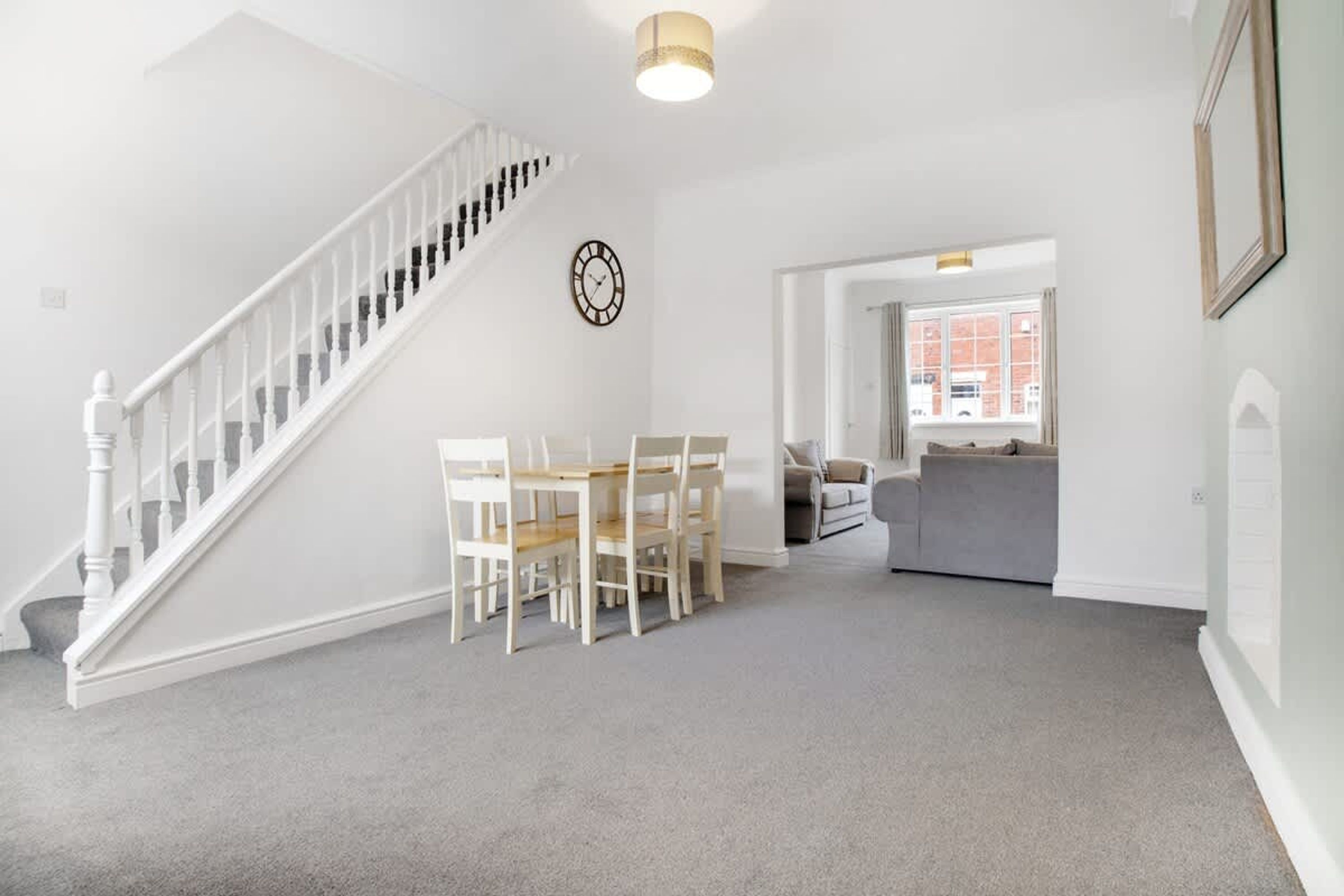 Uma sala ampla com escada, mesa de jantar com cadeiras, sofá e janela com vista para edifícios.