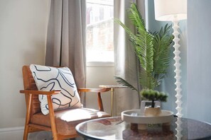 Quarto com cadeira de madeira, uma mesa pequena, um vaso de planta e uma luminária.