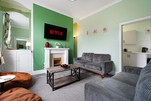 Uma sala de estar com lareira, sofá, mesa de centro e televisão exibindo 'NETFLIX'.