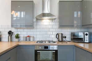 Cozinha moderna com eletrodomésticos de aço inoxidável, fogão a gás, forno e micro-ondas.