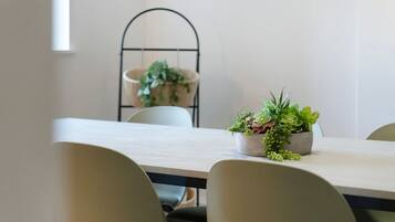 Uma mesa de jantar com cadeiras, uma planta em vaso e uma cesta suspensa com folhagem.