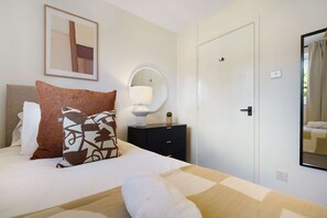 Quarto de hotel com cama, mesa de cabeceira com abajur, espelho e porta.