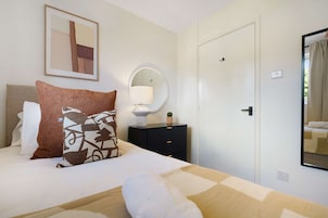 Quarto de hotel com cama, mesa de cabeceira com abajur, espelho e porta.