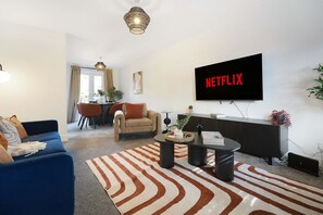 Uma sala de estar moderna com sofá, mesa de centro, TV na parede e uma área de jantar ao fundo.