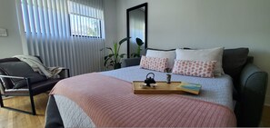 Quarto com cama, mesa de cabeceira, cadeira e janela com persianas.