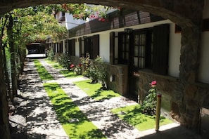 Um corredor com piso xadrez, paredes de pedra e uma fileira de janelas com persianas.