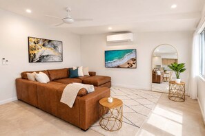 Uma sala de estar moderna com um sofá seccional, uma mesa de centro, um ventilador de teto, aparelho de ar condicionado e obras de arte nas paredes.