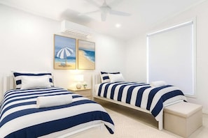 Quarto de hotel com duas camas, ventoinha no teto, pintura com tema praiano e uma janela grande.