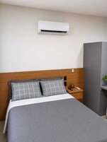 Quarto de hotel com cama, mesa de cabeceira, guarda-roupa e ar condicionado.