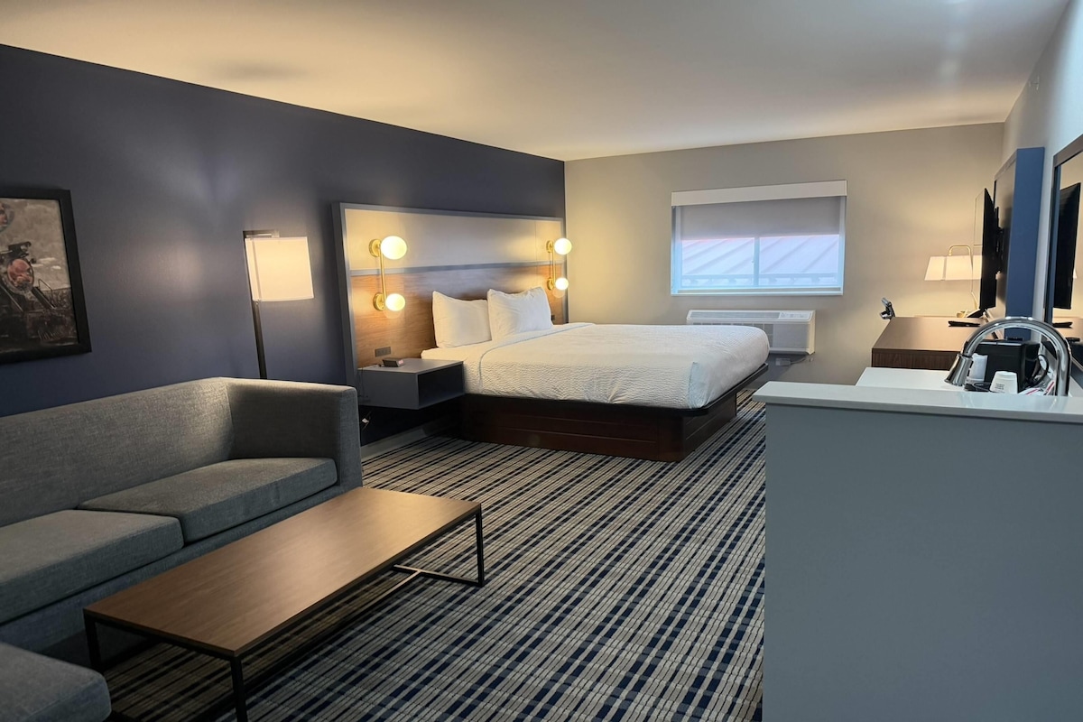 Quarto de hotel com cama, sofá, escrivaninha e televisão.