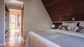 Quarto com teto inclinado, cama com cobre acolchoado e luminária de cabeceira.