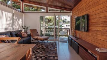 Interior moderno com teto de madeira, um sofá, uma poltrona, uma mesa de jantar e uma televisão na parede.